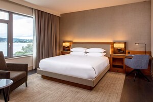 Quarto de hotel com uma cama grande, duas mesas de cabeceira com luminárias, uma cadeira e vista para um corpo de água.