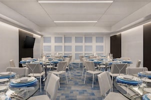 Uma sala de conferência com várias mesas preparadas para refeições, equipada com cadeiras e utensílios de mesa.