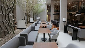 Uma área de refeições moderna em ambiente interno, com mesas compridas e assentos estofados em cinza.