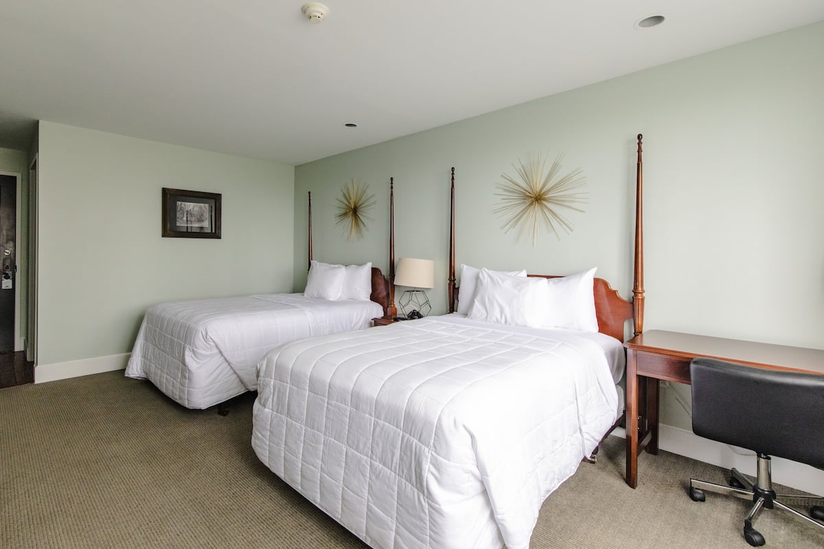 Quarto de hotel com duas camas, uma escrivaninha e uma cadeira.