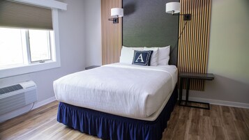 Cama bem arrumada com cabeceira branca, mesa de cabeceira e luminária fixada na parede.