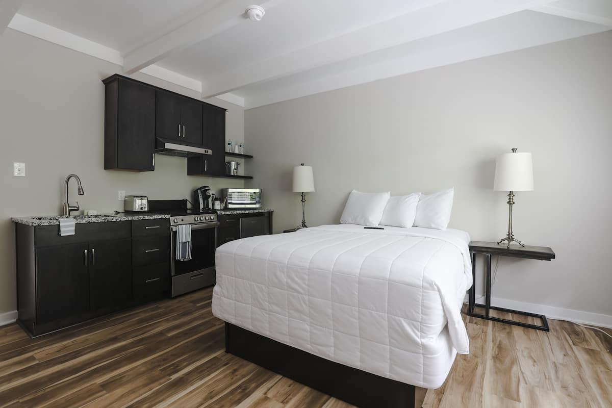 Quarto moderno com cama grande, cozinha planejada com armários escuros e mesa de cabeceira com luminárias.