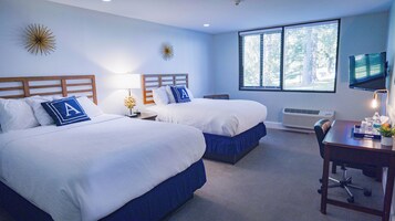Quarto de hotel com duas camas, uma escrivaninha, televisão e janela com persianas.