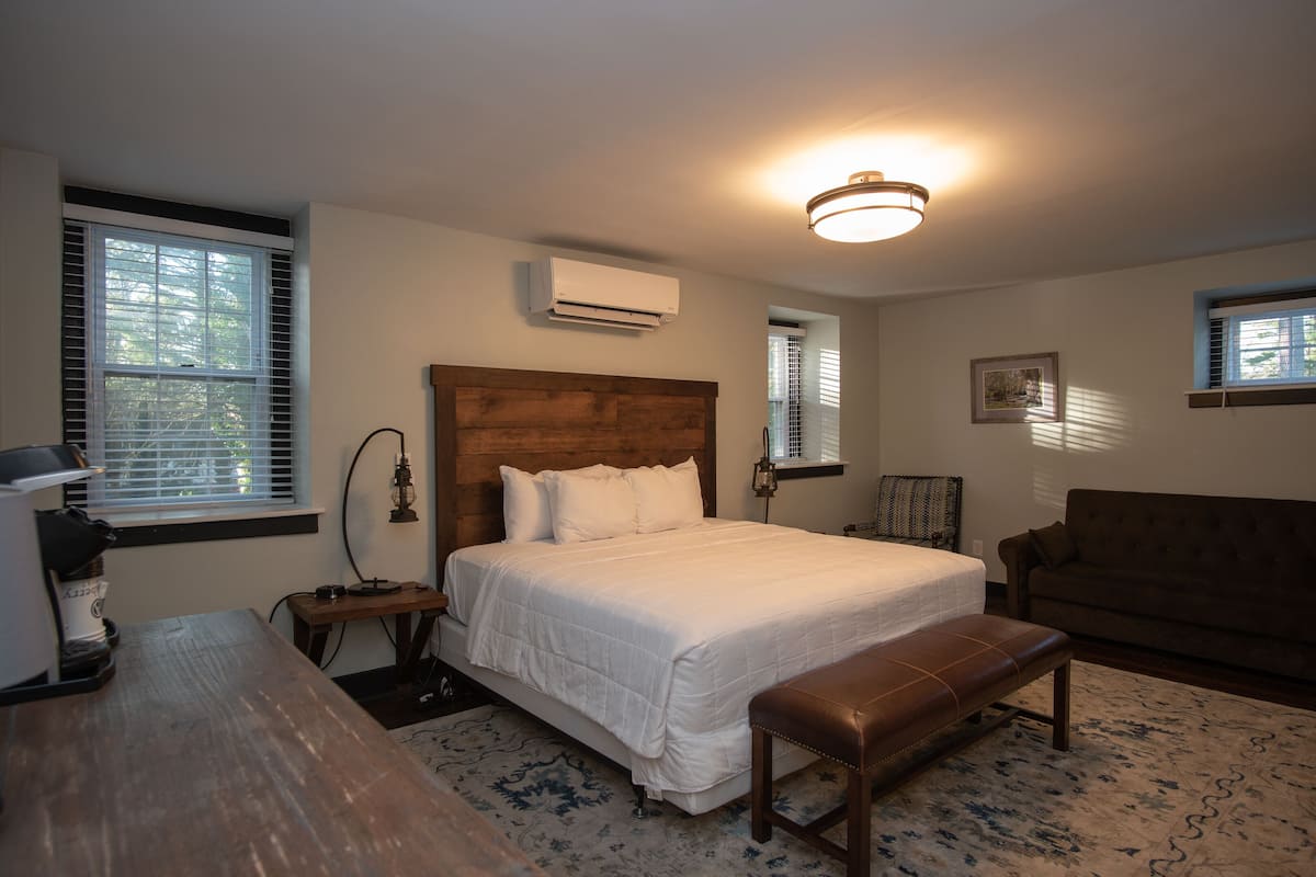 Um quarto com uma cama grande, uma cabeceira de madeira, um banquinho, uma escrivaninha e um sofá.