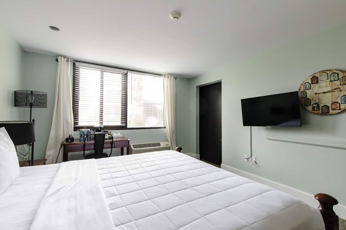 Quarto de hotel com uma cama grande, uma escrivaninha com cadeira, uma televisão fixada na parede e uma janela com persianas.