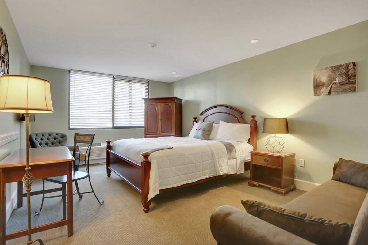Quarto com cama, mesas de cabeceira, cadeira, mesa e abajur.