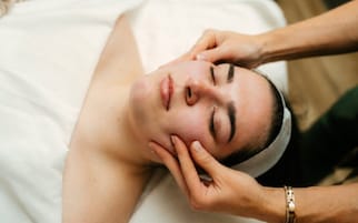 Uma pessoa deitada com as mãos no rosto, possivelmente recebendo um tratamento facial.