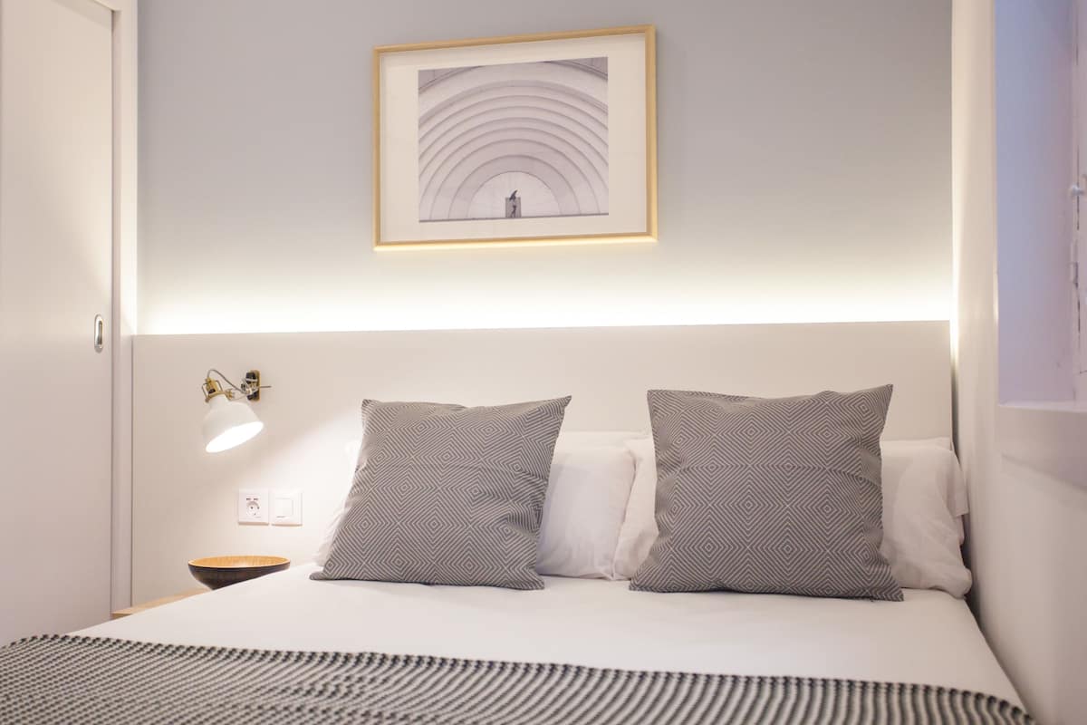 Uma cama bem arrumada com almofadas estampadas, um quadro emoldurado acima e uma luminária de cabeceira.