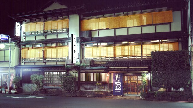 Um edifício tradicional japonês com vários andares, janelas amplas e uma placa.