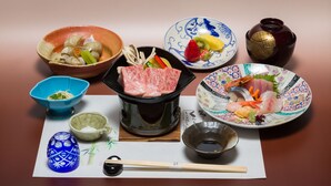 Diversos pratos, incluindo sashimi, legumes e um pote quente, dispostos sobre uma mesa com hashis e um bule de chá.