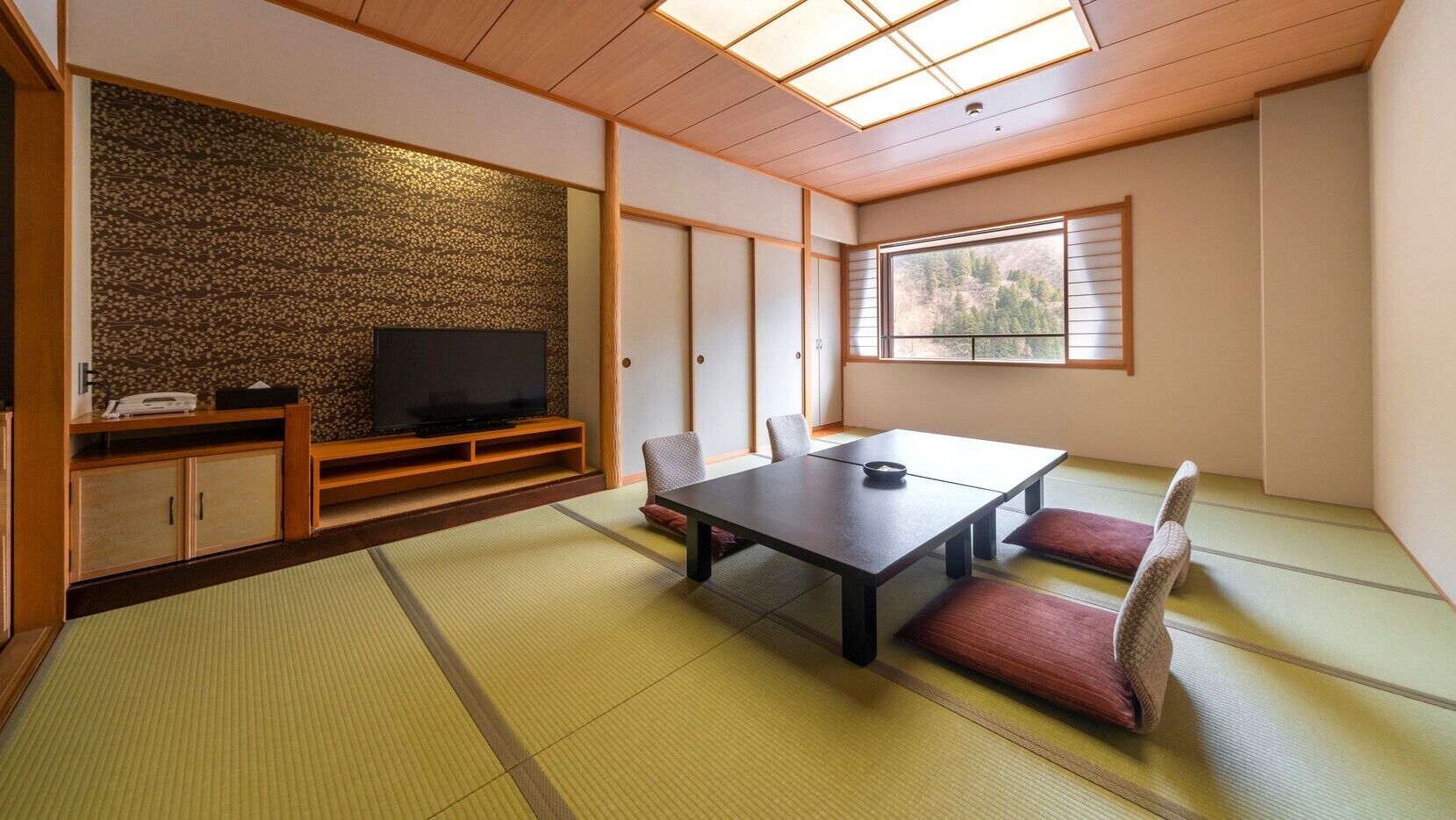 Um quarto japonês tradicional com tatames, uma mesa baixa, almofadas, televisão e uma porta de correr.