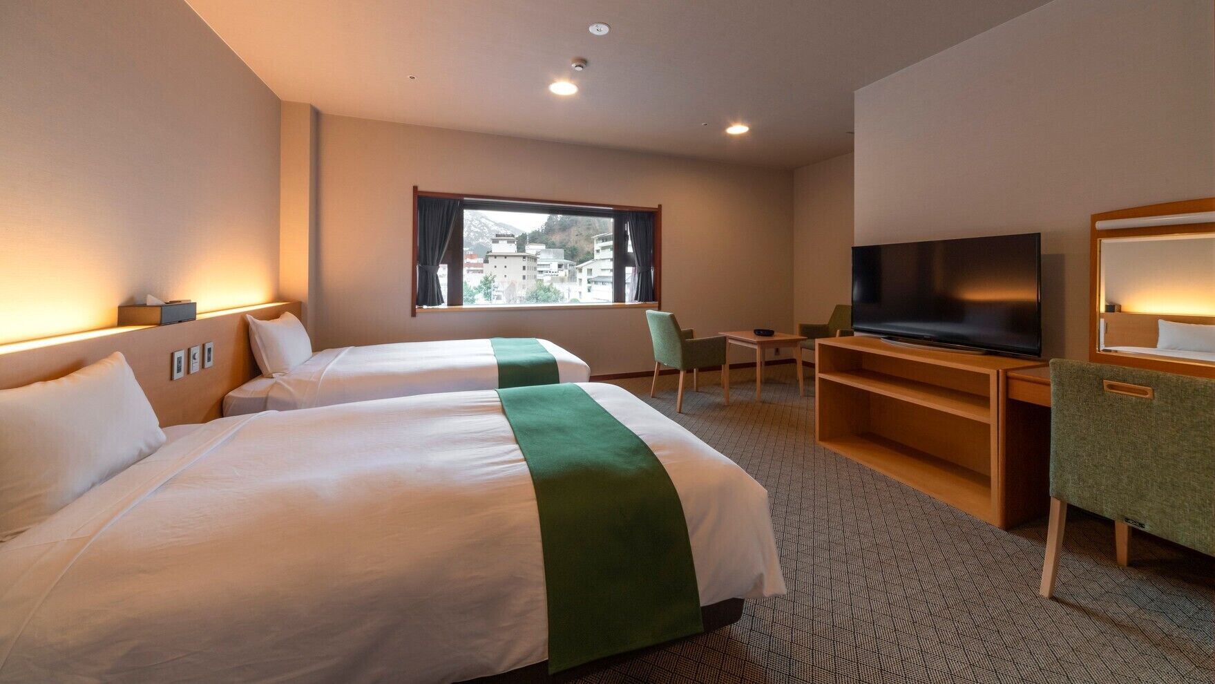 Quarto de hotel com duas camas, televisão, escrivaninha e janela com vista para edifícios.