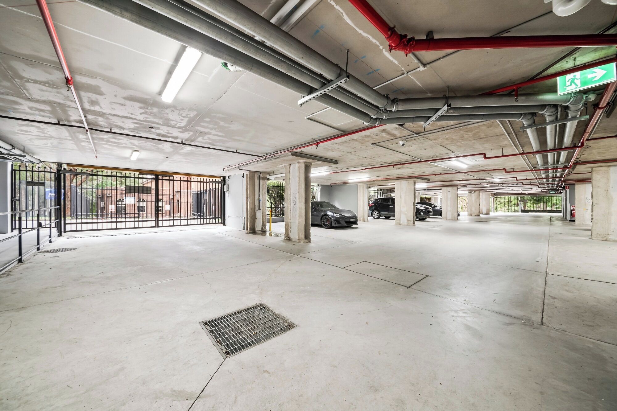 Um parque de estacionamento com vários níveis, pisos e pilares de concreto, entrada com portão e sinais de saída de emergência.
