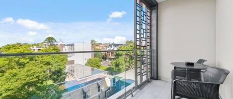 Varanda com vista para edifícios e árvores, uma mesa e uma cadeira.
