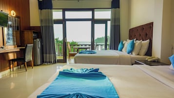 Quarto de hotel com duas camas, uma escrivaninha com computador, um refrigerador e vista para o oceano.