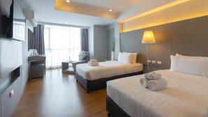 Quarto de hotel moderno com duas camas, uma escrivaninha, televisão de tela plana e uma janela grande com cortinas.
