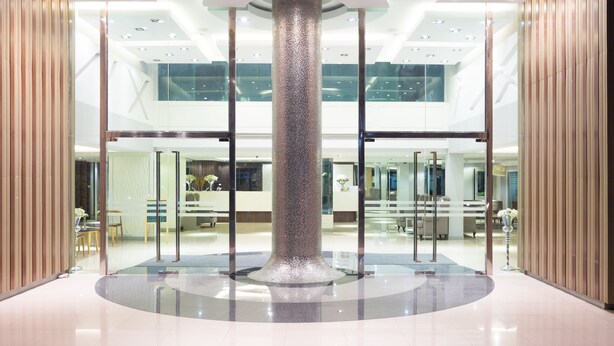 Um hall moderno com uma coluna central, portas de vidro e um teto alto com iluminação embutida.