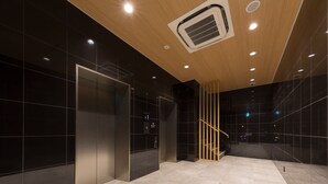 Um elevador moderno com visor digital, escada de ripas de madeira e chão de azulejos escuros.