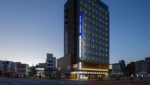 Um hotel moderno com vários andares, entrada destacada e sinalização iluminada.
