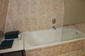 Um banheiro com banheira, porta-toalhas com toalhas e uma garrafa de shampoo.