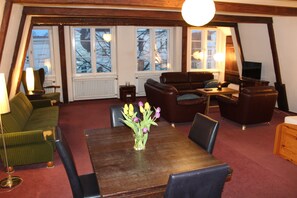 Uma sala de estar acolhedora com uma mesa de jantar de madeira, sofá verde e poltronas de couro marrom.