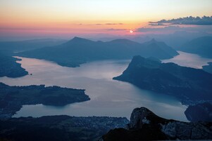 Vista panorâmica de uma paisagem montanhosa, com um rio e uma cidade na base.