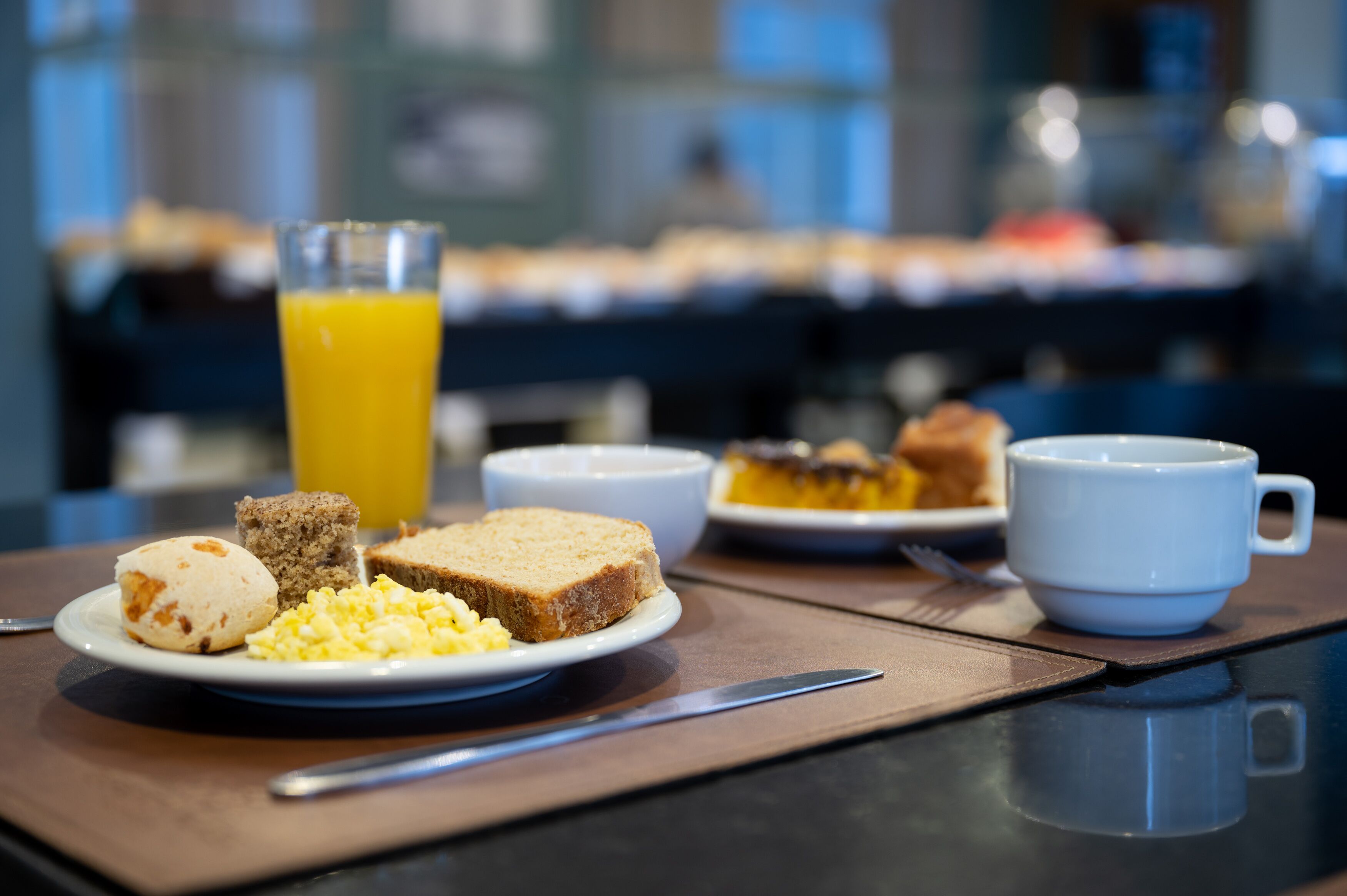 Uma mesa posta para o pequeno-almoço, com torradas, ovos mexidos e um copo de sumo de laranja.