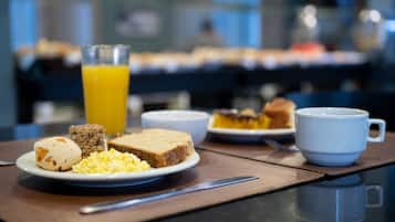 Uma mesa posta para o pequeno-almoço, com torradas, ovos mexidos e um copo de sumo de laranja.