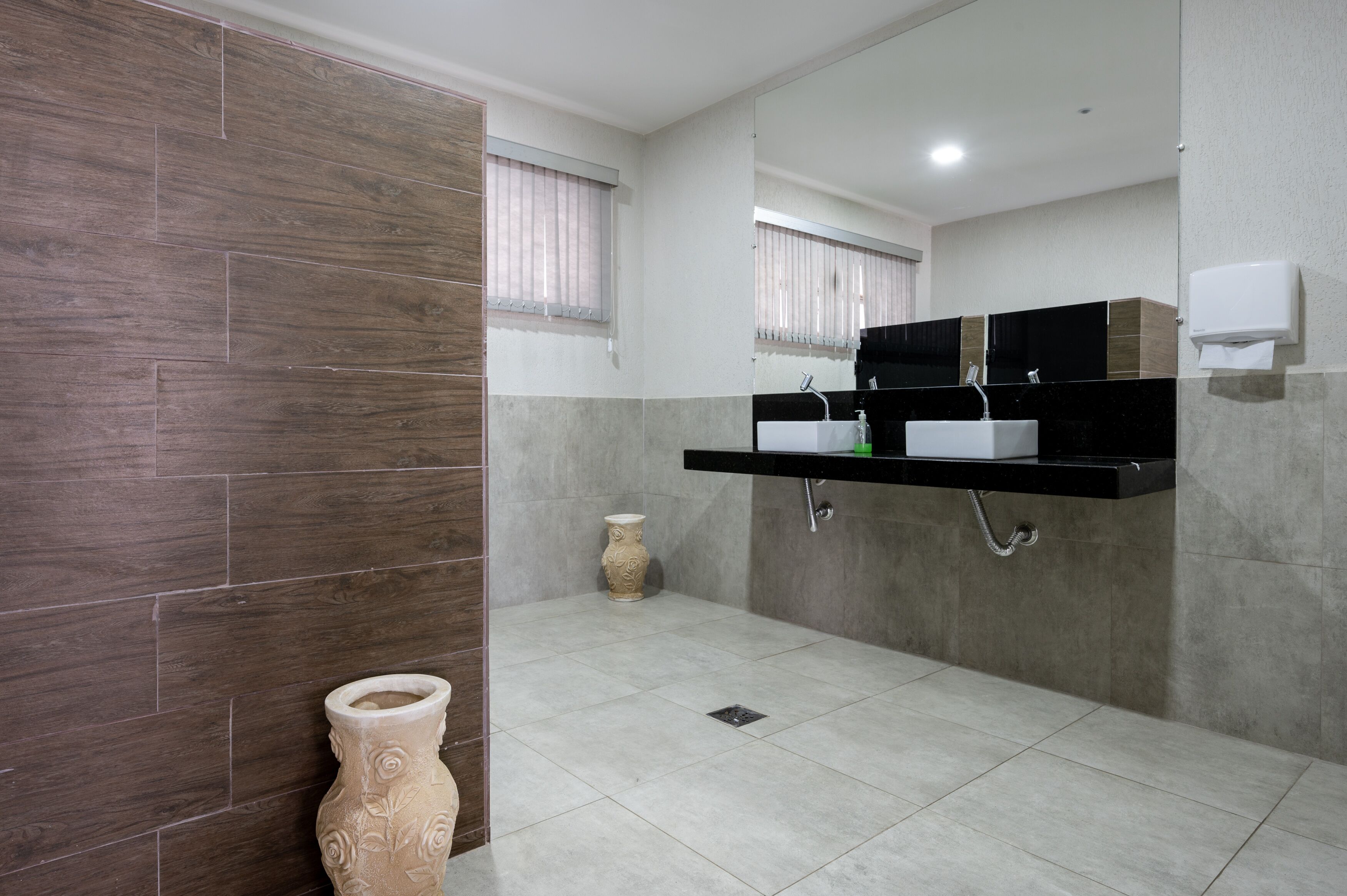 Um banheiro moderno com um espelho grande, uma bancada preta com uma pia e um vaso decorativo.
