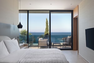 Quarto com cama grande, televisão e varanda com vista para o mar.