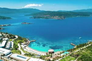 Um resort costeiro com piscina, praia e montanhas ao fundo.