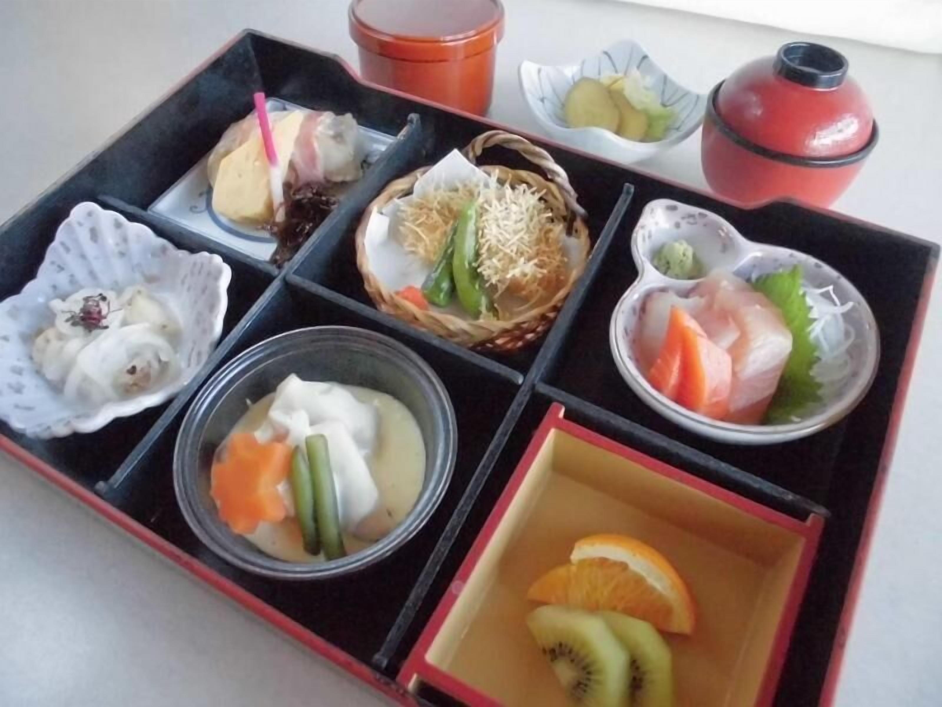Uma lancheira bento com diversos alimentos, incluindo sushi, legumes e frutas.