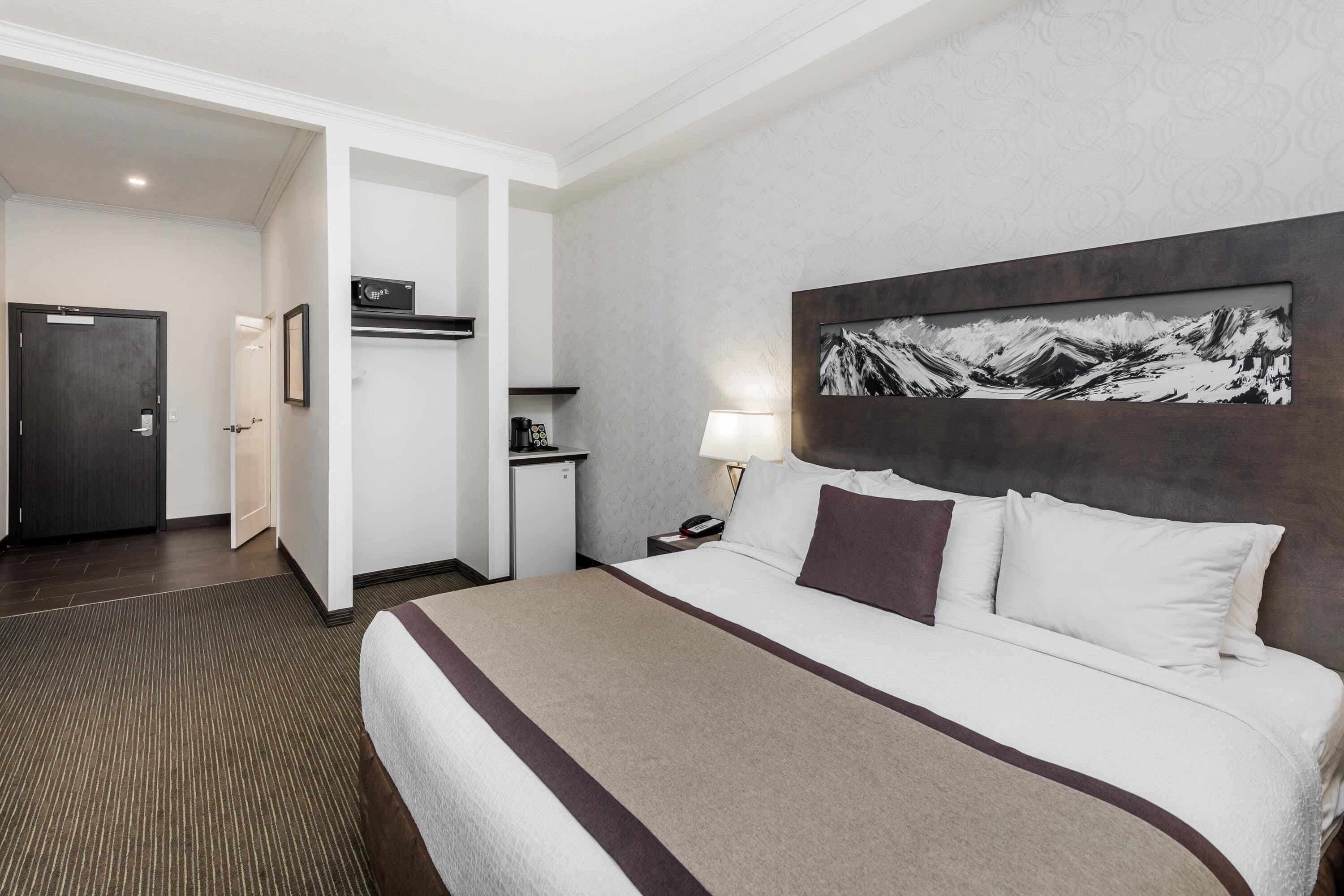 Quarto de hotel com cama grande, mesa de cabeceira, escrivaninha, porta e uma obra de arte pendurada na parede.
