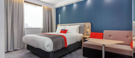 Quarto de hotel com cama, mesa pequena e sofá.