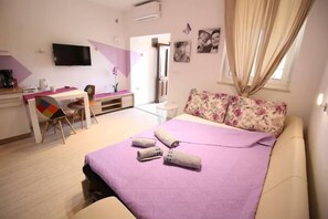 Um quarto com uma cama, escrivaninha, cadeira e televisão.