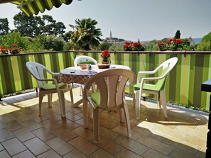 Um pátio externo com uma mesa redonda e quatro cadeiras, um cercado listrado e uma vista para o horizonte urbano ao fundo.