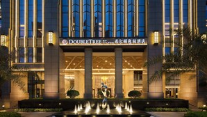 Entrada de hotel com uma fonte, colunas imponentes e sinalização iluminada.