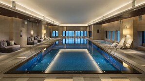 Uma grande piscina interior com espreguiçadeiras e sofás de ambos os lados, janelas amplas e design moderno.