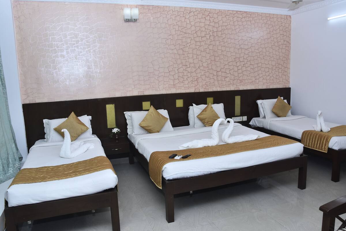 Quarto de hotel com três camas, cada uma com a toalha disposta em formato de cisne, parede estampada e cabeceira de madeira.