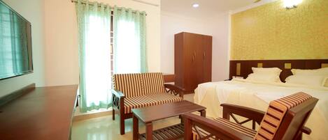 Quarto de hotel com cama, uma cadeira de madeira, mesa de madeira, guarda-roupa e ventilador de teto.