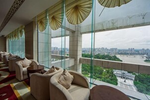 Quarto de hotel com grandes janelas, vista para a cidade e varanda com assentos.