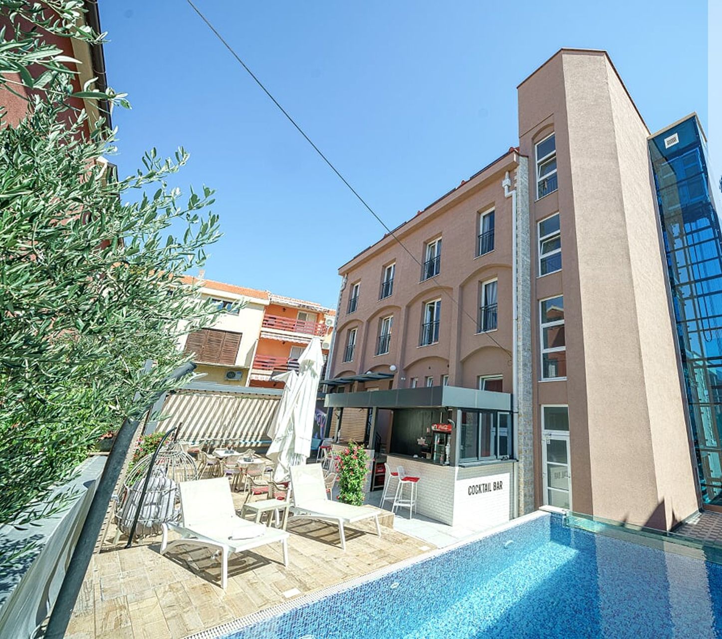 Um hotel com área de piscina, bar de cocktails e vista para os edifícios ao redor.
