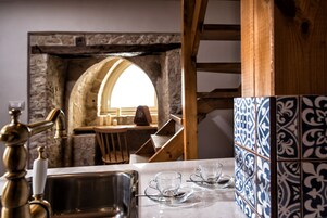 Cozinha com parede de pedra, viga de madeira e painel de azulejos.