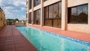 Piscina adjacente a um edifício com janelas amplas e um caminho pavimentado com azulejos.