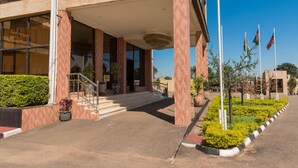 Um edifício com entrada coberta, degraus que levam até ele e um mastro com bandeiras.