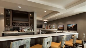 Uma área de bar moderna com um balcão comprido, banquetas e uma televisão.