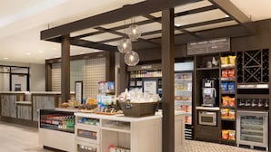 Um hall de hotel com estação de bebidas de serviço próprio, uma vitrine refrigerada e uma máquina de café.
