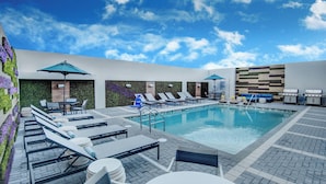 Área da piscina com espreguiçadeiras, mesa e churrasqueira.