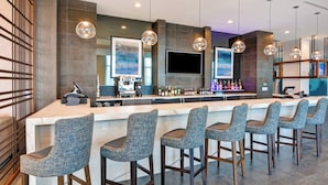 Uma área de bar moderna com bancada de mármore, banquetas, luminárias pendentes e uma televisão de tela plana.