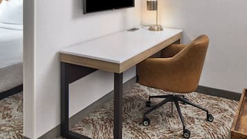 Quarto de hotel com cama, escrivaninha, cadeira, televisão e abajur.